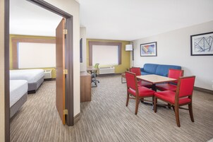 Quarto de hotel com duas camas, uma escrivaninha, uma mesa com cadeiras vermelhas e um sofá azul.