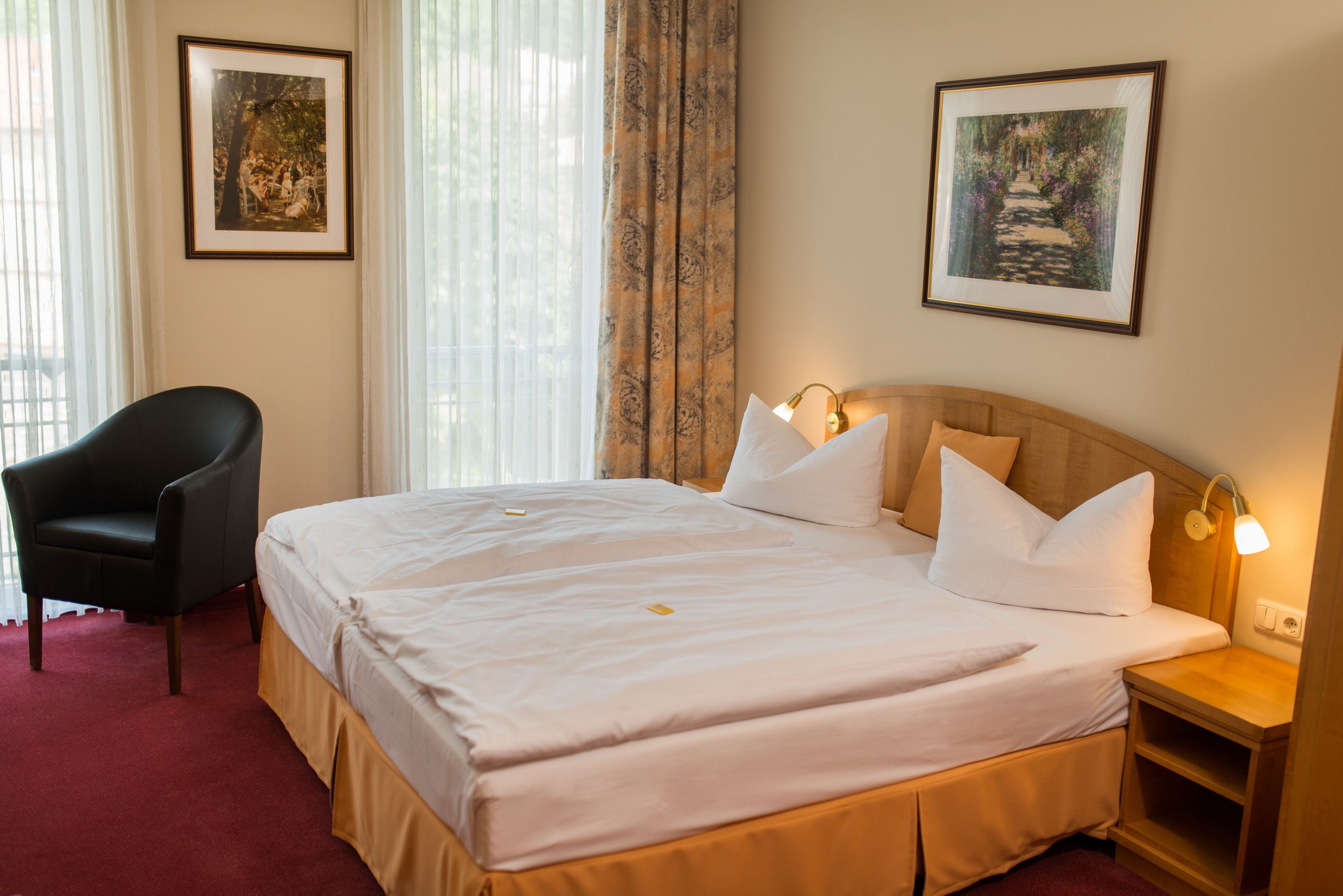 Quarto de hotel com uma cama grande, uma cadeira e duas imagens emolduradas nas paredes.