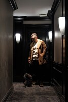 Um homem num casaco parado num corredor com um cachorro.