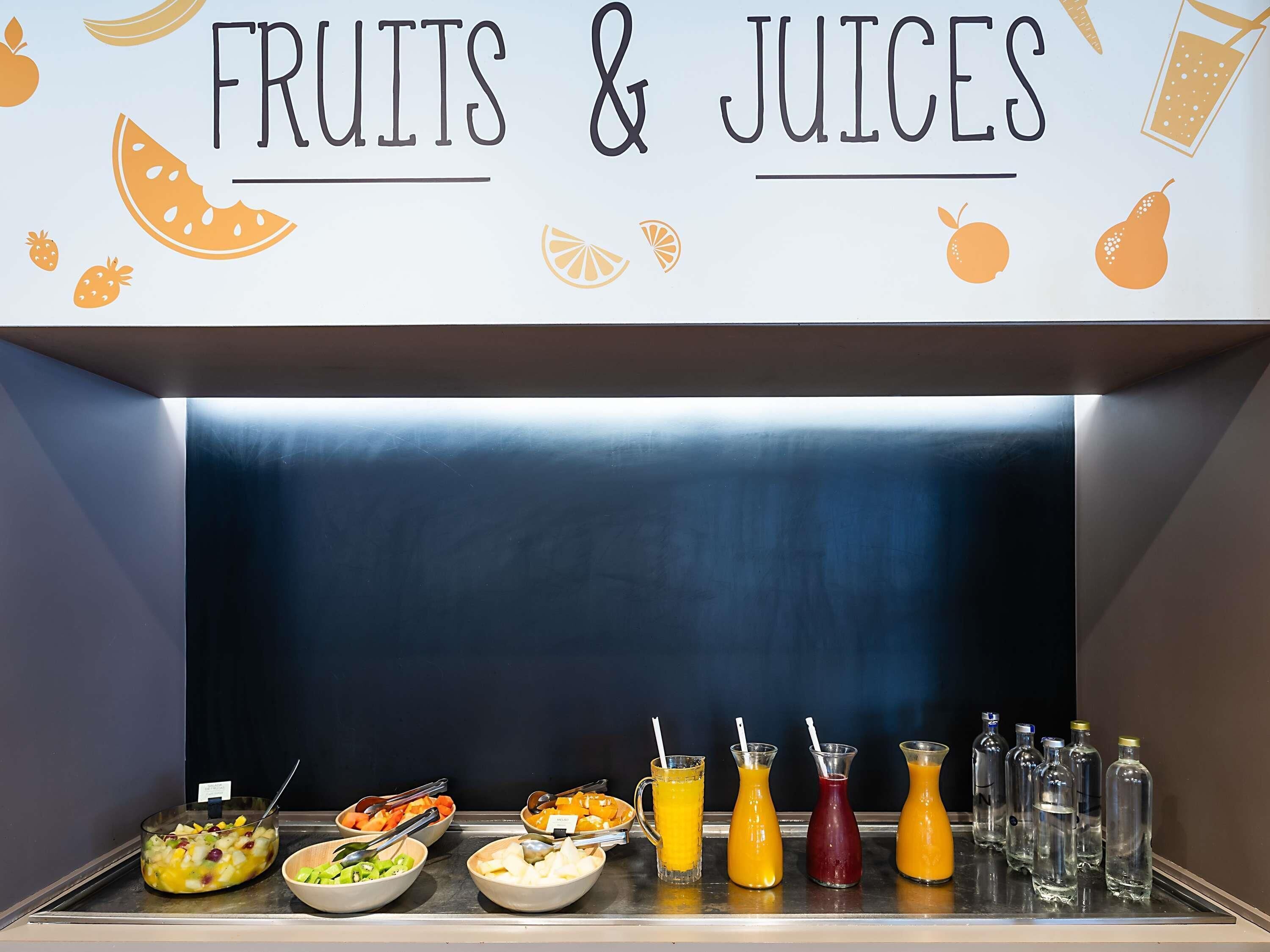 Buffet com frutas e sucos, incluindo potes de fruta, jarra de suco de laranja e garrafas de água.