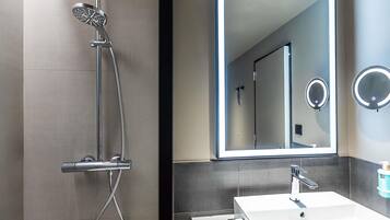 Uma casa de banho moderna com chuveiro, um espelho grande e uma pia.