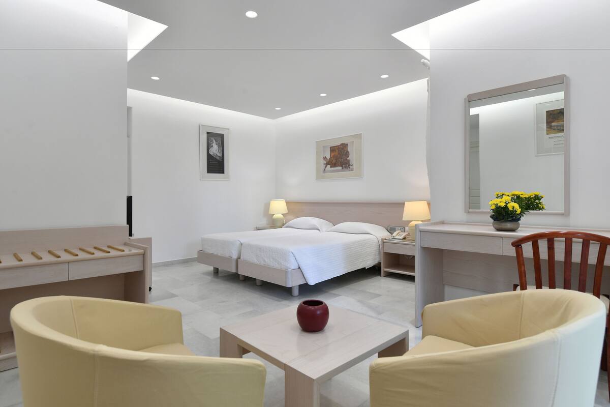 Quarto de hotel moderno com cama, escrivaninha, cadeiras e uma pequena mesa com um vaso.