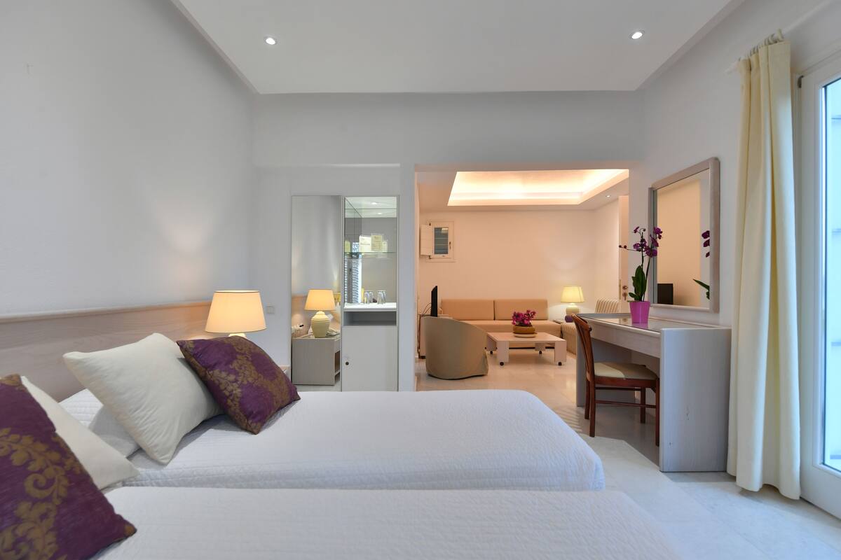 Quarto de hotel com cama, mesa de cabeceira, luminária, cadeira, escrivaninha e espelho.