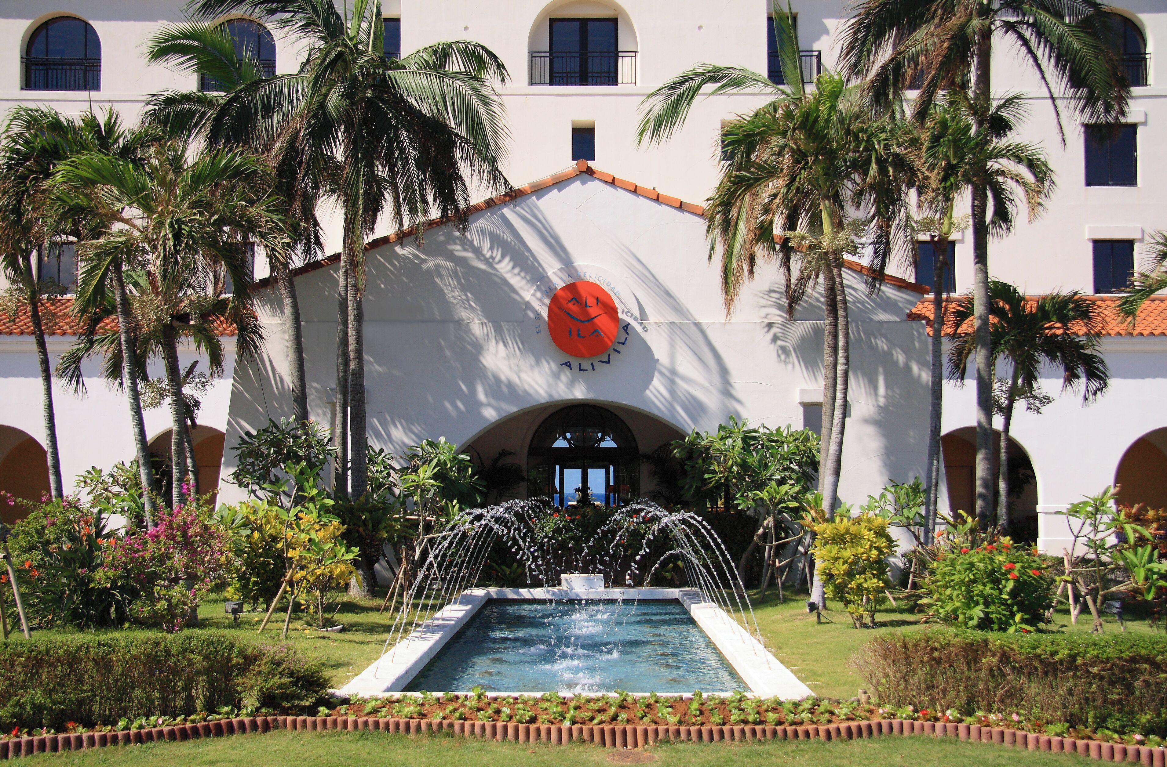 Um edifício com piscina, palmeiras e uma fonte.