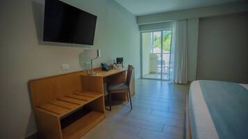 Quarto de hotel com cama, escrivaninha com cadeira, televisão na parede e vista para o exterior através de uma porta de vidro deslizante.