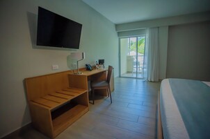 Quarto de hotel com cama, escrivaninha com cadeira, televisão na parede e vista para o exterior através de uma porta de vidro deslizante.