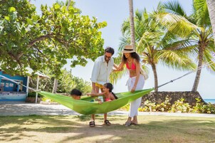 Uma família relaxando em uma rede em um cenário tropical, com palmeiras e céu claro.