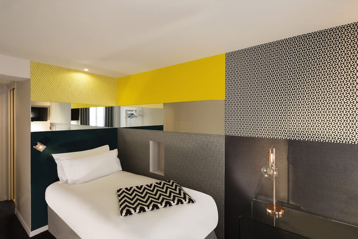Quarto de hotel moderno com cama, mesa de cabeceira e espelho.