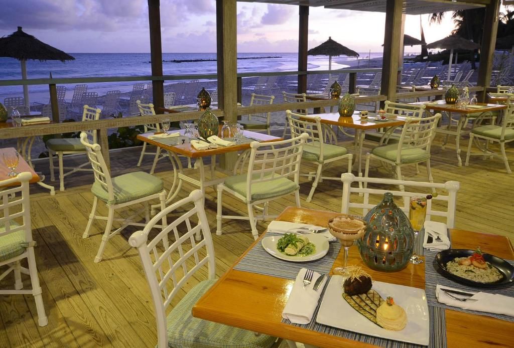 Um restaurante com mesas e cadeiras, vista para o oceano e uma praia ao fundo.