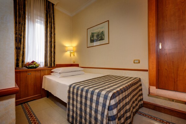 Quarto de hotel com cama, mesa de cabeceira, abajur, quadro na parede e porta de madeira.