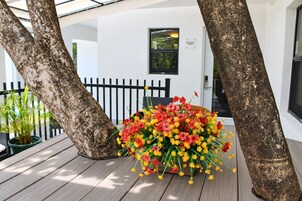 Um deck de madeira com um arranjo de flores, uma cerca de metal preto e um edifício com uma placa indicando uma sala de café da manhã.