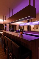 Uma área de bar moderna com um balcão comprido, banquetas e teto iluminado por neon.