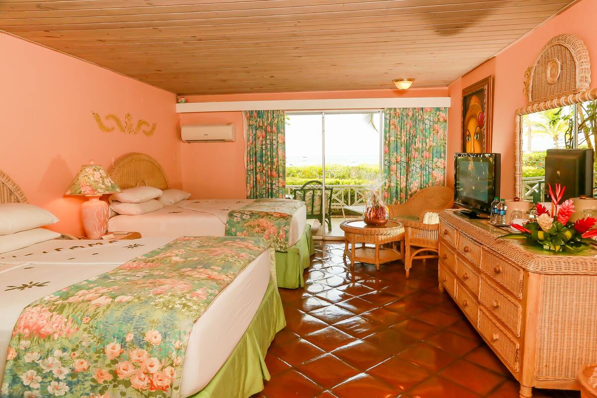 Quarto de hotel com duas camas, televisão, cômoda e varanda com vista.