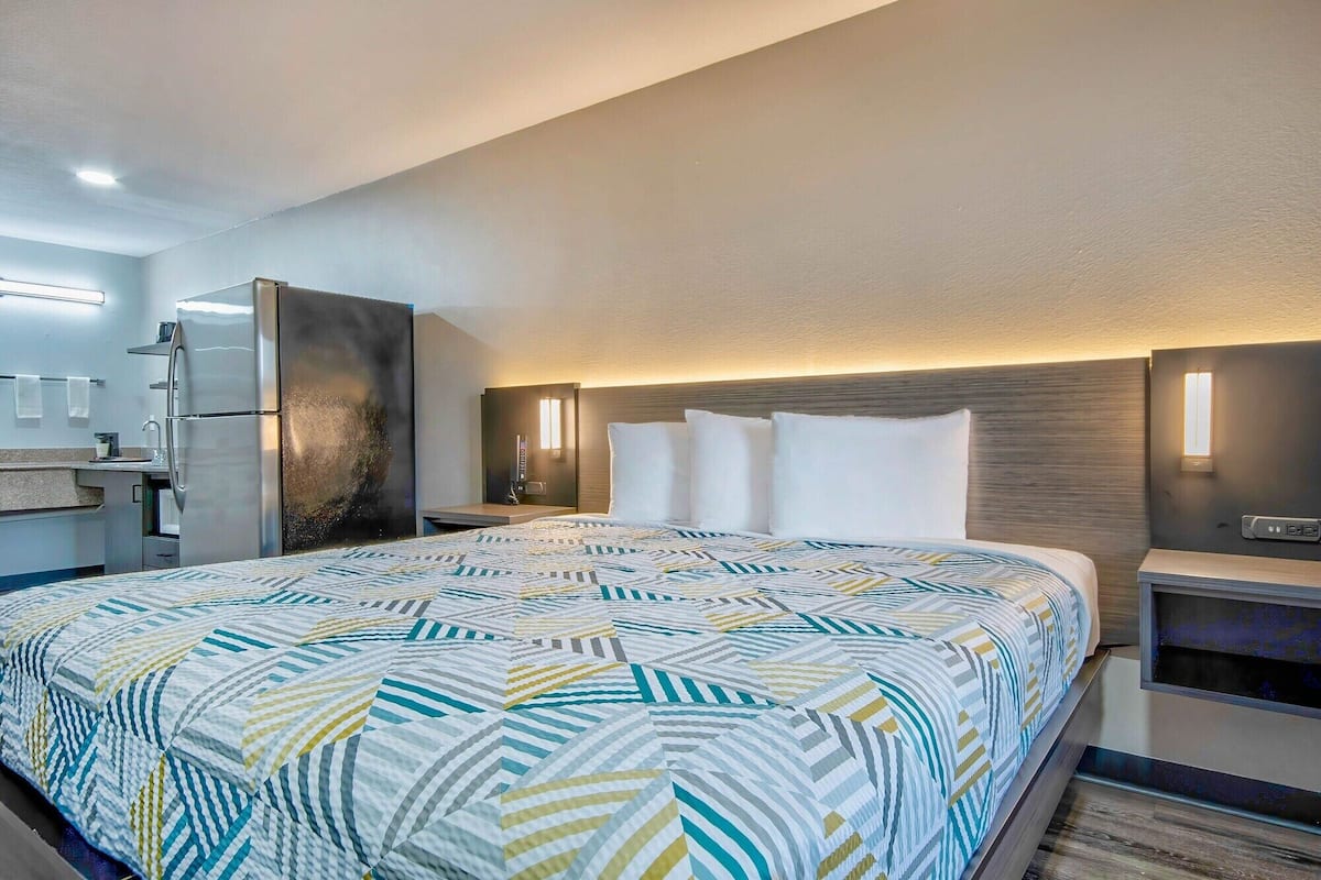 Quarto de hotel com uma cama grande, um frigorífico, uma pia e um espelho.