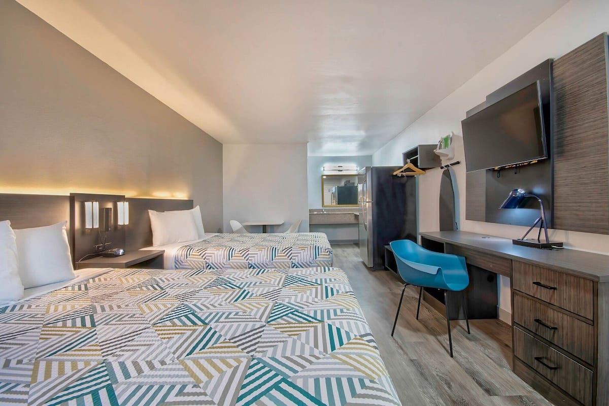 Quarto de hotel com uma cama grande, uma escrivaninha com cadeira, um espelho e uma televisão.