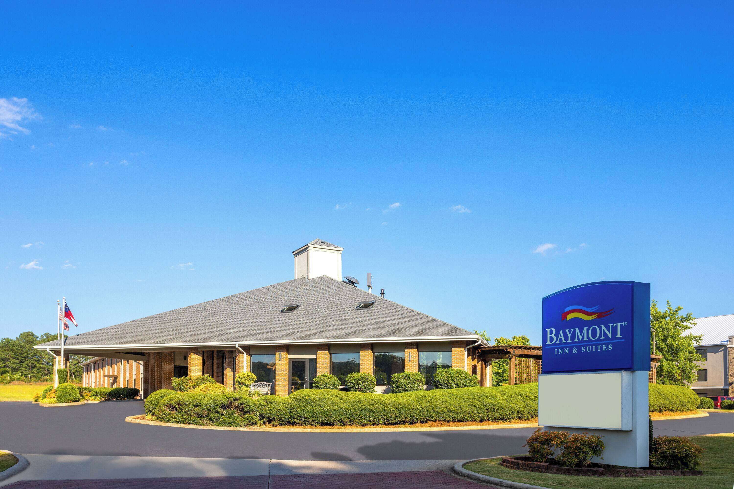 Edifício do Baymont Inn & Suites com fachada de tijolos, entrada coberta e gramado bem cuidado.