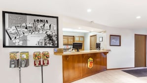 Uma área de recepção com um balcão de madeira, um quadro com a placa de boas-vindas e três máquinas de moedas.