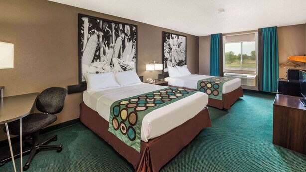 Quarto de hotel com duas camas, uma mesa, uma cadeira e uma luminária de mesa.