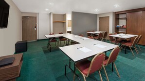 Uma sala de conferências com mesas compridas, cadeiras e piso coberto de carpete.