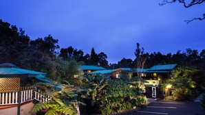 Um hotel com telhado verde, cercado por vegetação exuberante e um estacionamento.