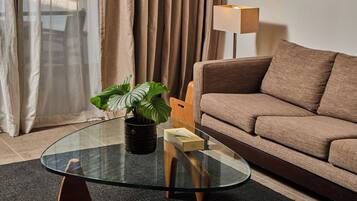 Uma sala de estar moderna com uma mesa de centro de vidro, um sofá marrom, uma planta em vaso e um abajur.