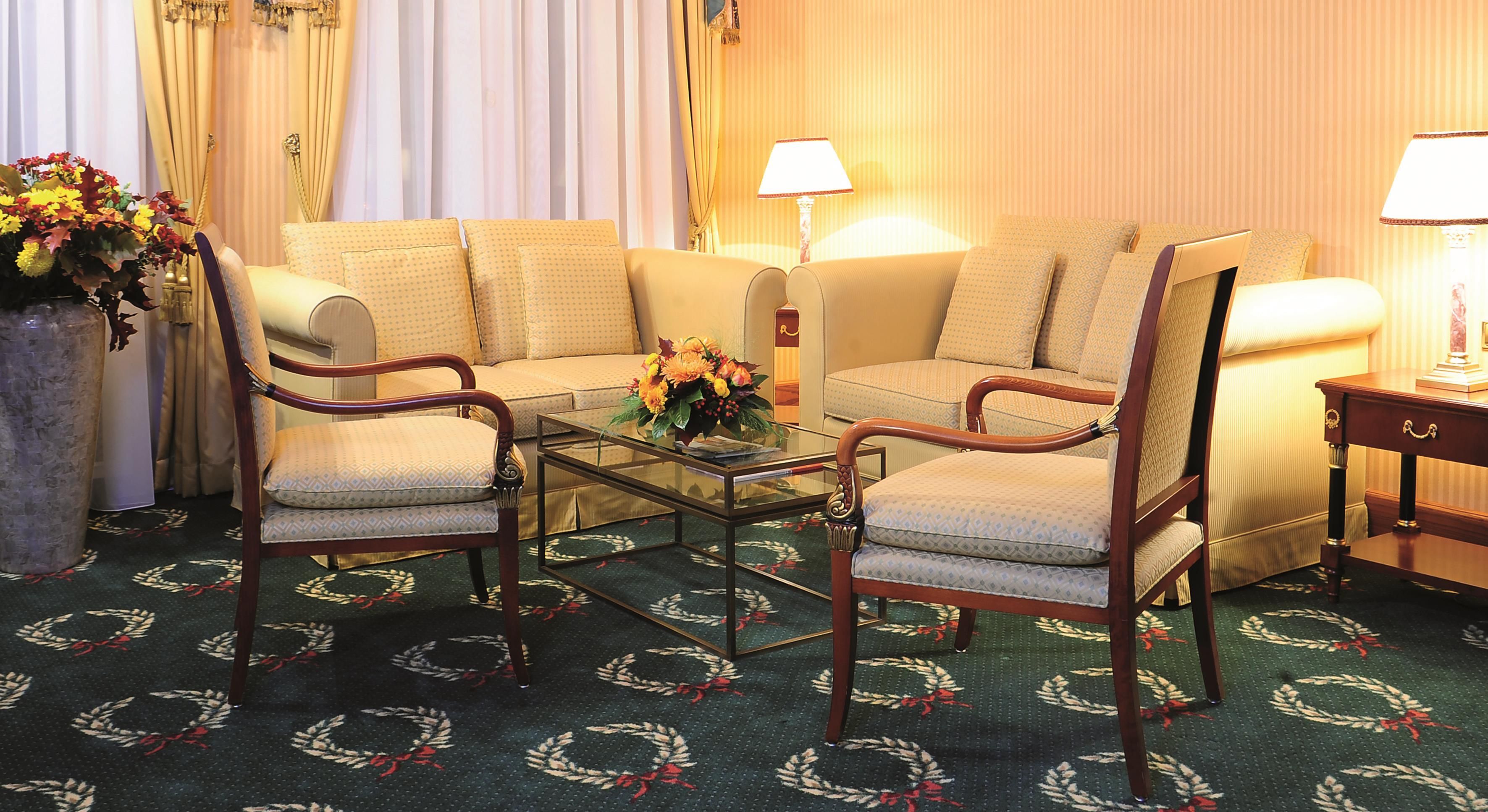 Quarto com sofá, duas poltronas, mesa de centro de vidro e mesa lateral com luminária.