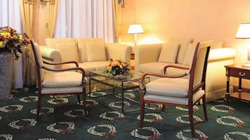 Quarto com sofá, duas poltronas, mesa de centro de vidro e mesa lateral com luminária.