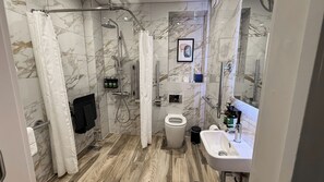 Uma casa de banho moderna com chuveiro, sanita, lavatório e paredes de mármore.