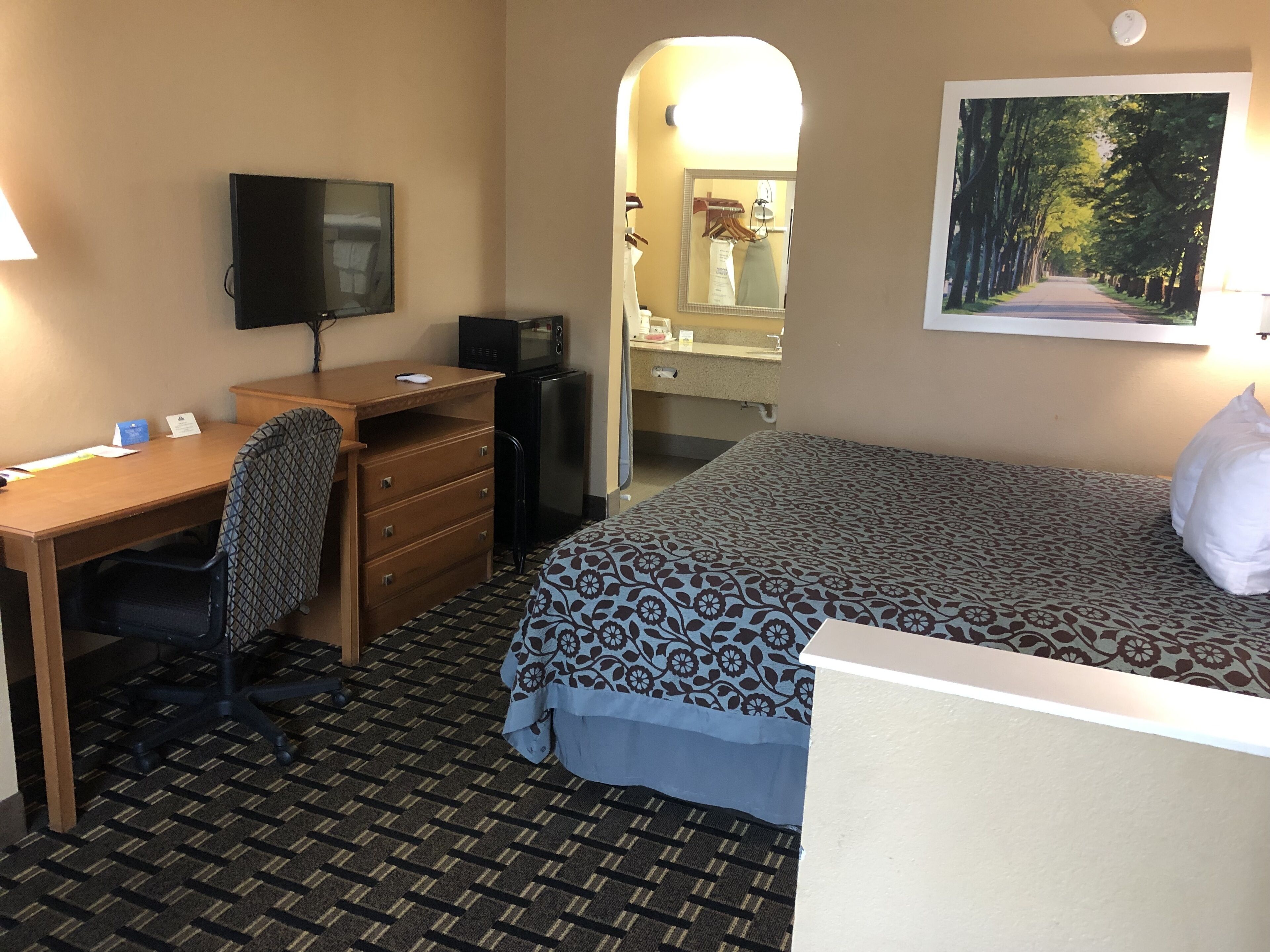 Quarto de hotel com escrivaninha, cadeira, cama e televisão.
