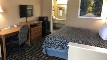 Quarto de hotel com escrivaninha, cadeira, cama e televisão.