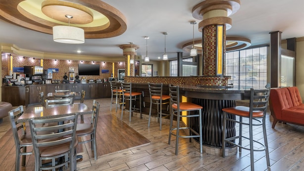 Uma área de bar moderna com uma ilha central, banquetas e um espaço de estar com um sofá.