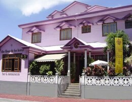 Um hotel com fachada roxa, um bar e restaurante no andar térreo, e uma placa indicando ser o Hotel Fleur de Lys.