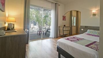 Quarto com cama, escrivaninha, cadeira, mesa pequena e porta de vidro deslizante para área externa.