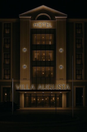 Um hotel chamado 'Villa Augusta', com arquitetura clássica, destacando uma entrada imponente e grandes janelas.