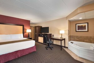 Quarto de hotel com cama, escrivaninha, cadeira, televisão e banheira.