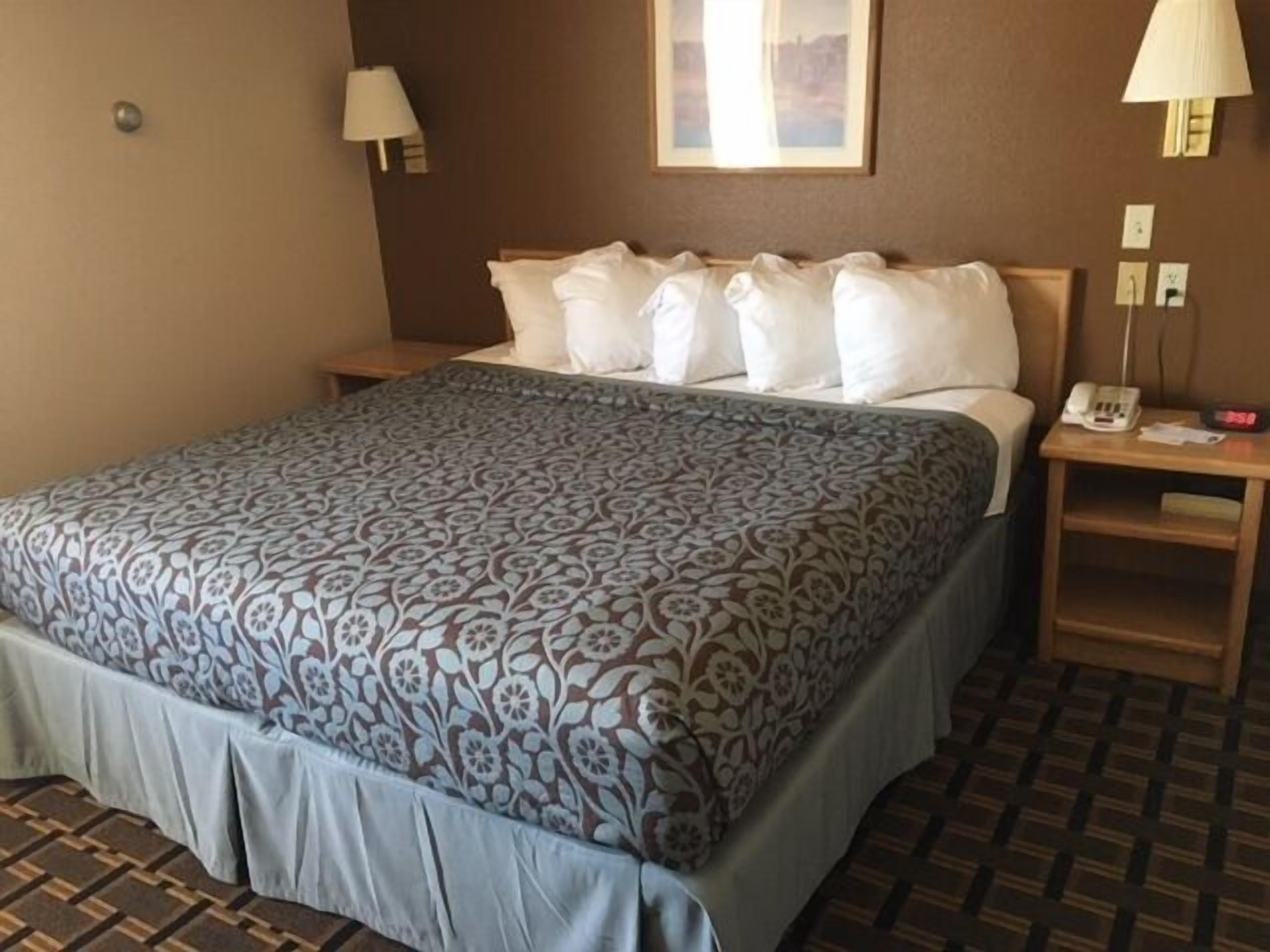 Quarto de hotel com cama, mesa de cabeceira, abajur e quadro na parede.