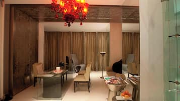 Uma sala de estar moderna com uma mesa de centro de vidro, um sofá e uma mesa de jantar com uma vela. Há um candelabro sobre a mesa de centro e um abajur no canto.
