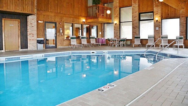 Uma piscina interior com espreguiçadeiras e mesas, paredes de madeira e um ventilador de teto.