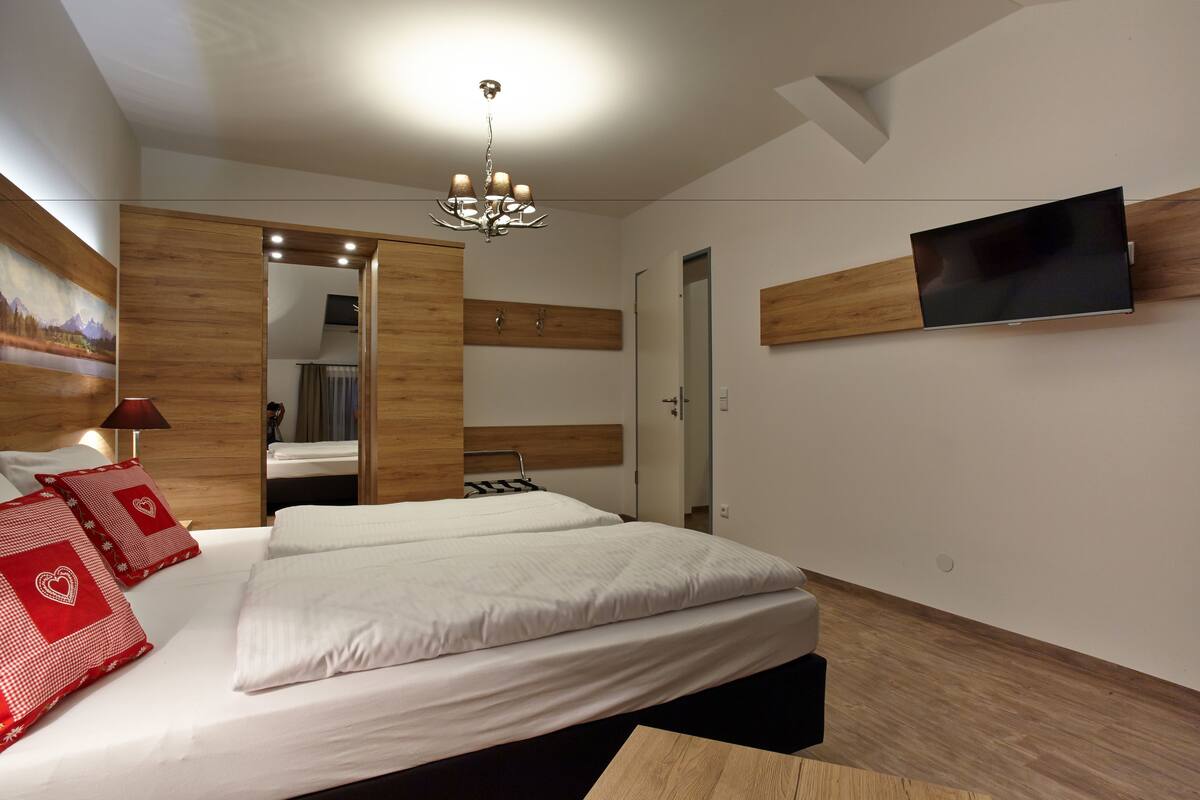 Quarto de hotel moderno com uma cama grande, uma TV fixada na parede e um painel de parede em madeira.