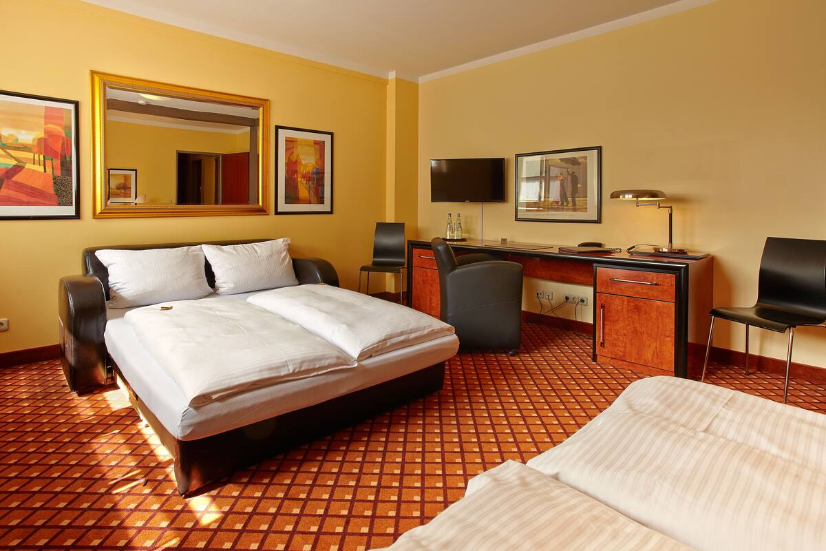 Quarto de hotel com uma cama grande, uma mesa com cadeira, televisão e obras de arte nas paredes.