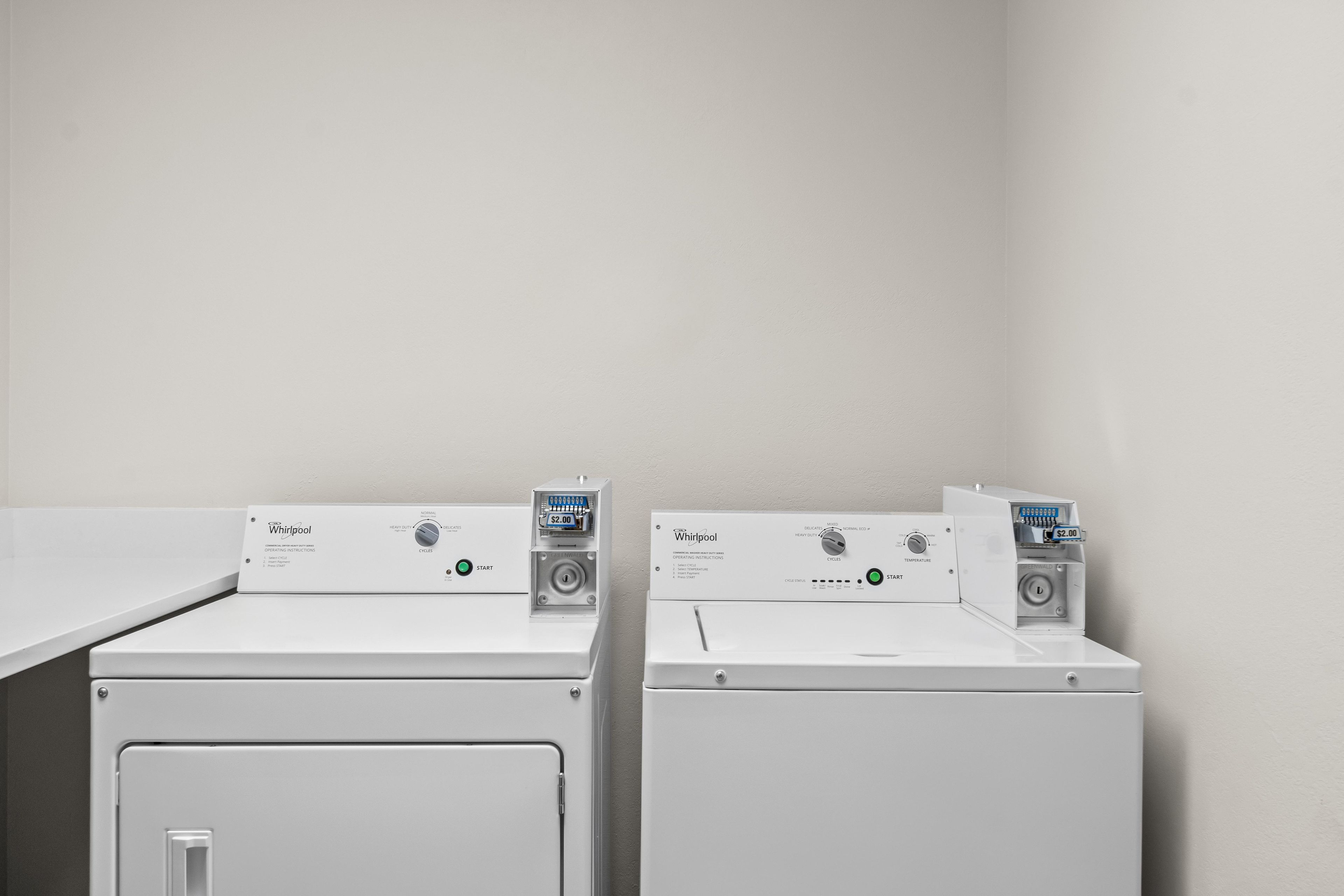 Duas máquinas de lavar Whirlpool brancas numa lavanderia com uma parede lisa.