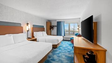Quarto de hotel com duas camas, uma escrivaninha, televisão e janela com vista.