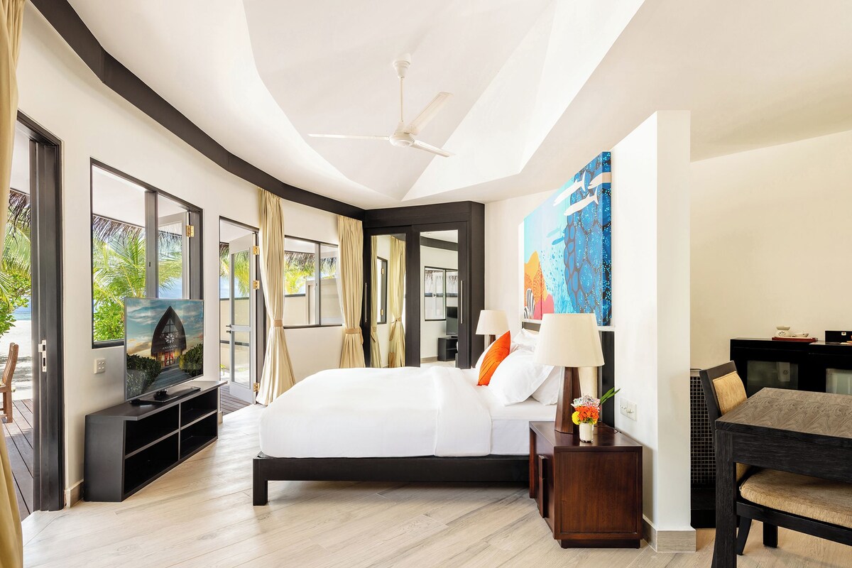 Quarto de hotel moderno com uma cama grande, um ventilador de teto, uma TV e uma área de refeições.