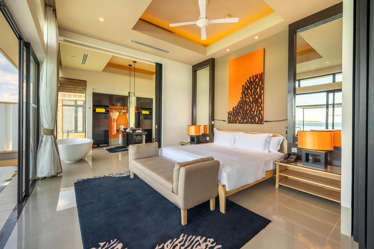 Quarto de hotel moderno com uma cama grande, área de estar, banheira e vista para o mar.