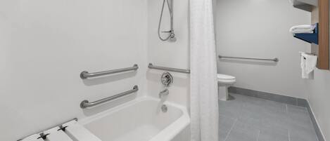 Casa de banho moderna com banheira, chuveiro e sanita. Inclui barras de apoio e porta-toalhas.