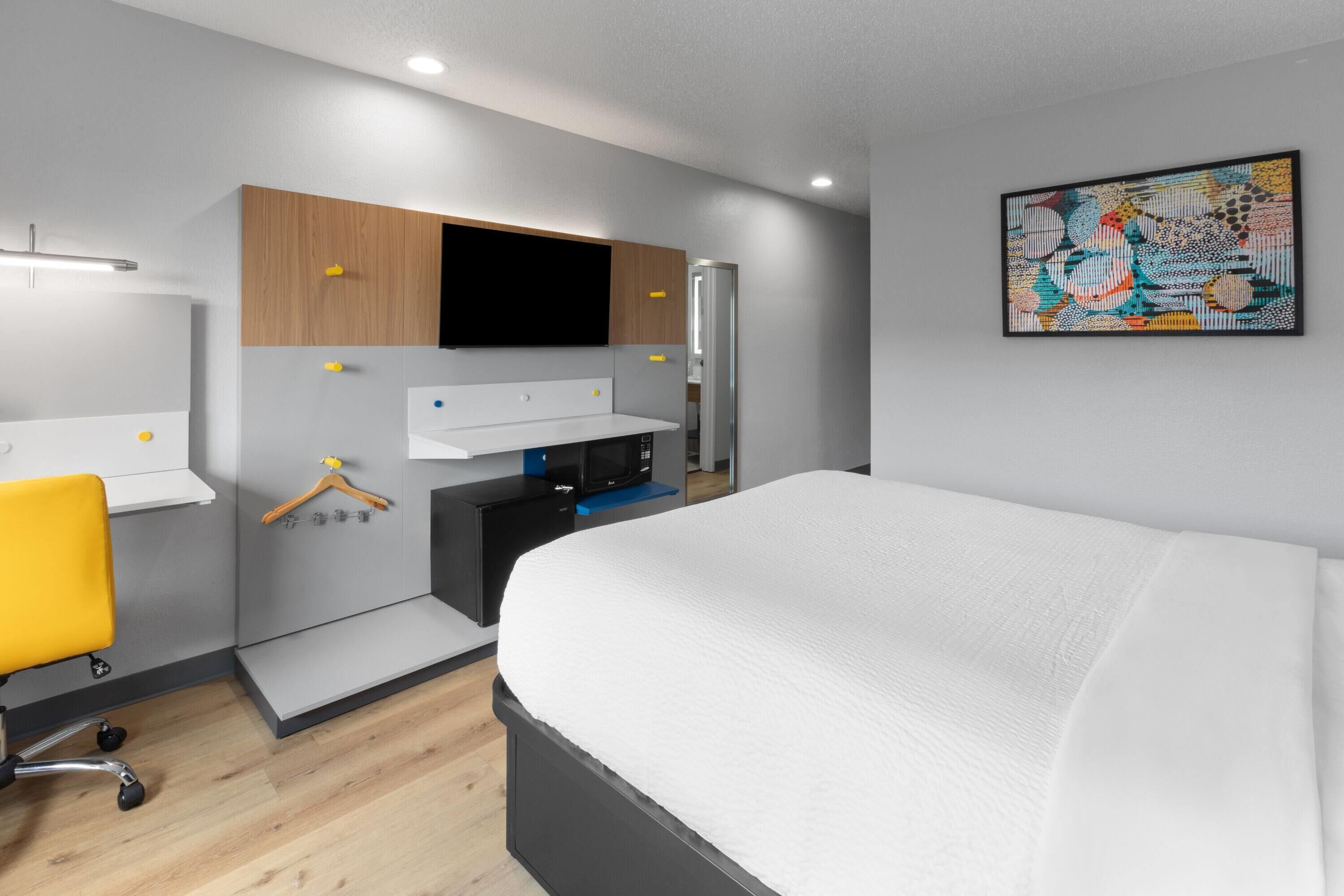 Quarto de hotel moderno com cama, escrivaninha, cadeira, televisão de tela plana e espelho de banheiro.