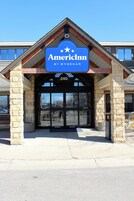 Entrada do AmericInn by Wyndham, com fachada de pedra, uma placa azul com estrelas e o número 240.