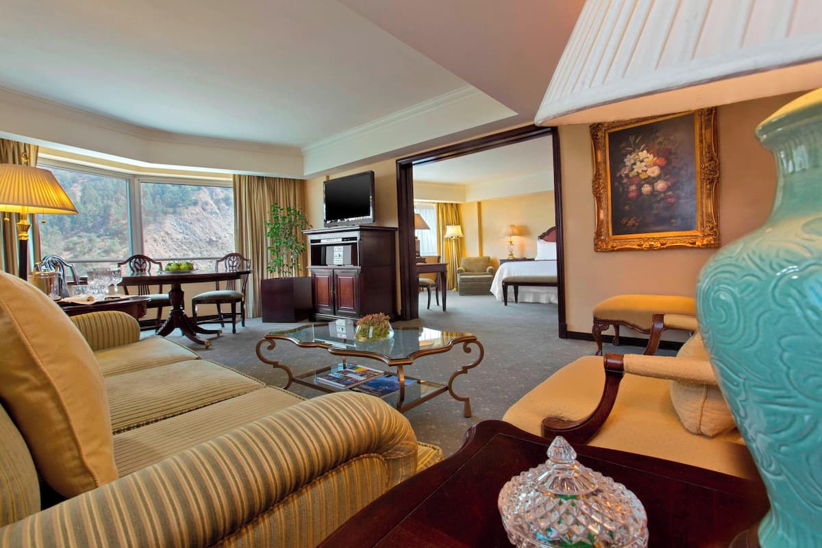 Quarto de hotel com sofá, poltrona, mesa de jantar e televisão.