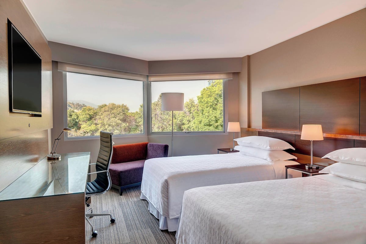 Quarto de hotel com duas camas, uma escrivaninha, uma cadeira e uma televisão.