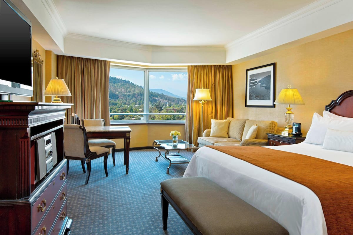 Quarto de hotel com uma cama grande, uma mesa com cadeira, televisão e vista para o exterior.